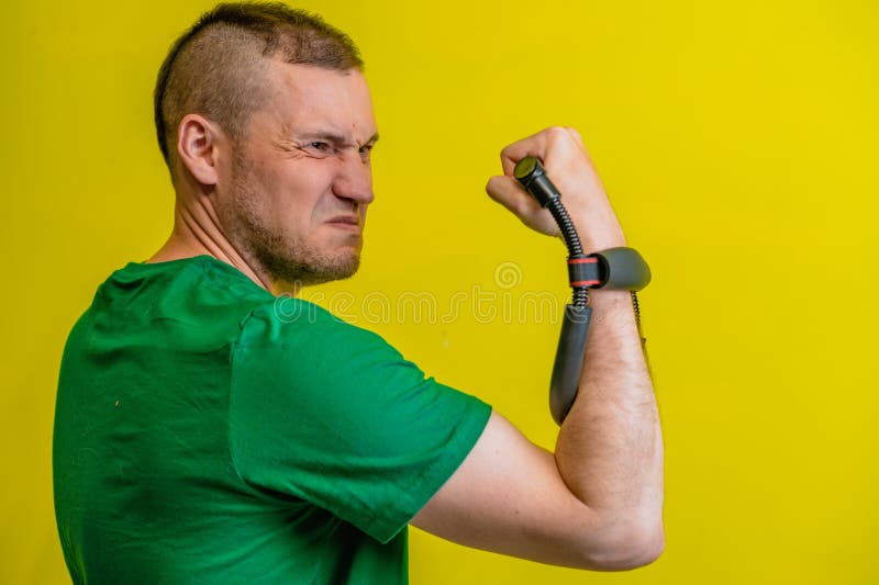 Determined Man Flexing Bicep with Hand Grip Exerciser Against Yellow ...