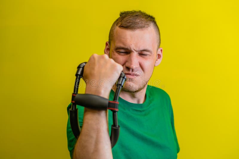 Determined Man Flexing Bicep with Hand Grip Exerciser Against Yellow ...