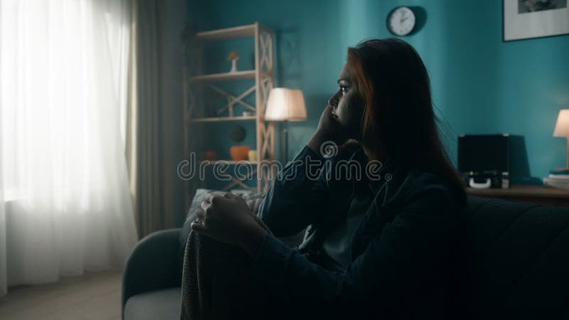 A Devastated, Distant, Lonely Young Woman Sits on a Sofa in a Dark Room ...