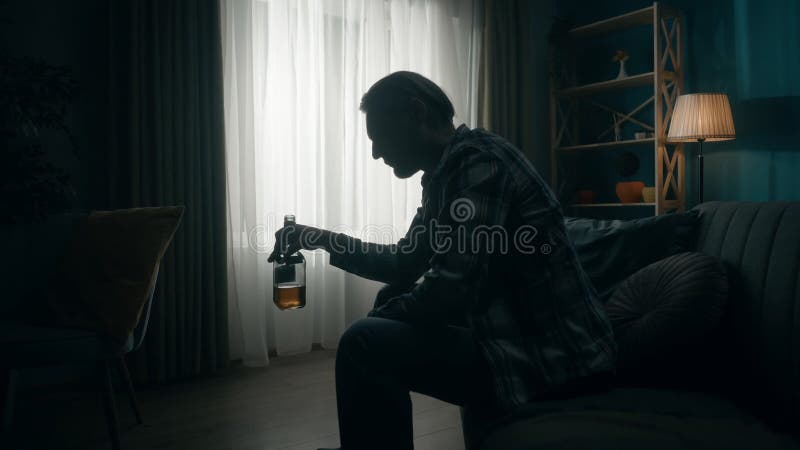 A Devastated Man Sits in a Dark Room with a Bottle of Alcohol. Side ...