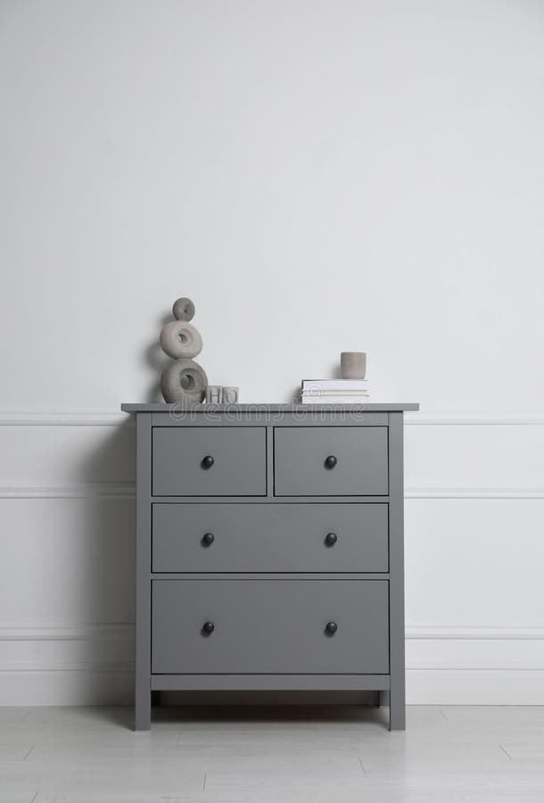 Different Accessories on Grey Chest of Drawers Near White Wall Indoors ...