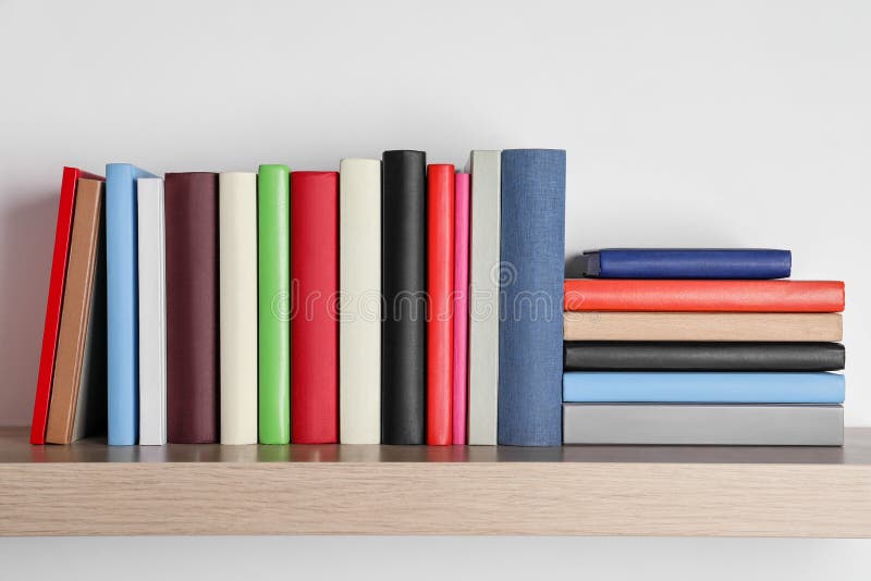 Different Books on Wooden Shelf Near White Wall Stock Image - Image of ...