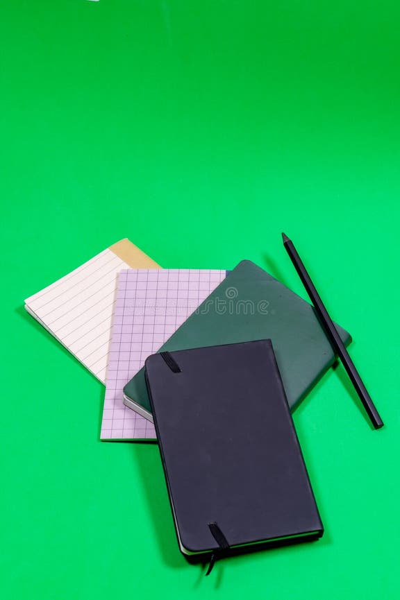 Different Types of Colored Notebooks with a Black Pen on a Green ...