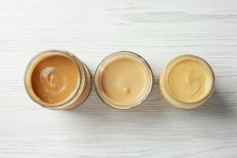 Different Types of Spicy Mustard in Glass Jars on White Wooden Table ...