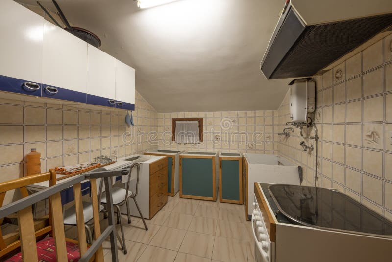 Dilapidated Kitchen with Mixed Furniture and Chairs Stacked in a Corner ...