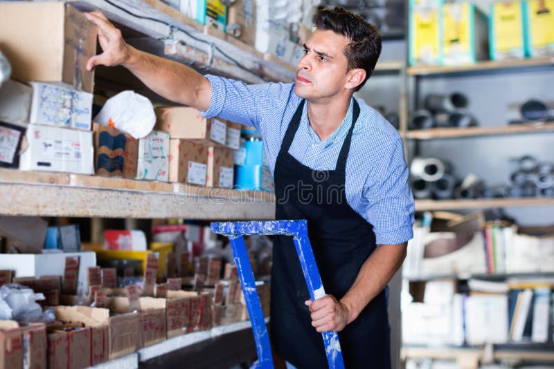Man in Unifom is Using Ladder To Reach the Top Shelves in the Building ...