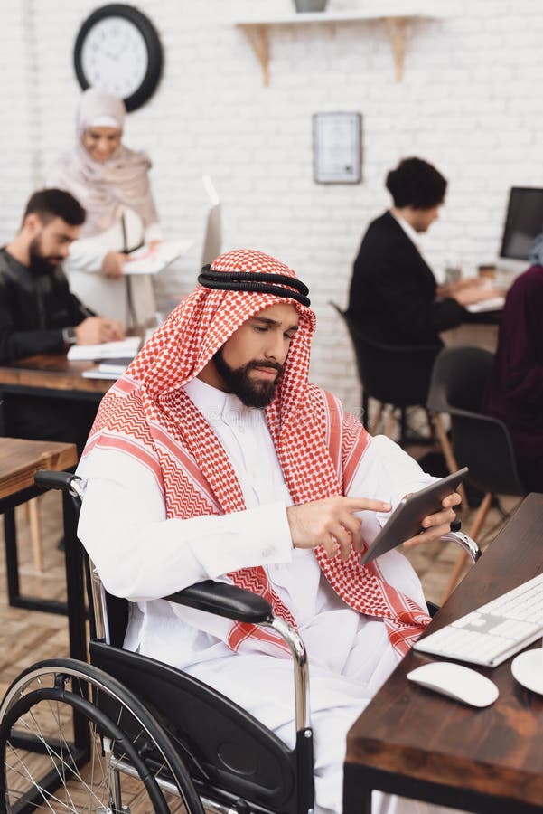 Disabled Arab Man In Wheelchair Working In Office Man Is Using Tablet