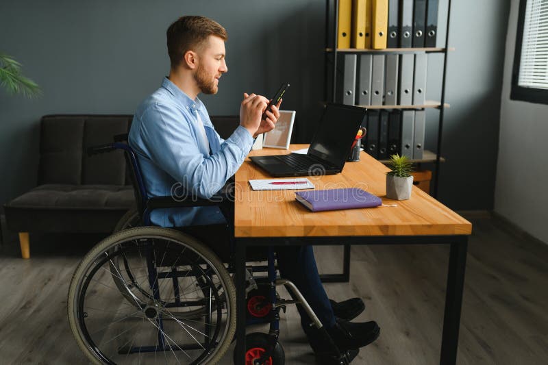 Disabled Person in the Wheelchair Works in the Office at the Computer ...