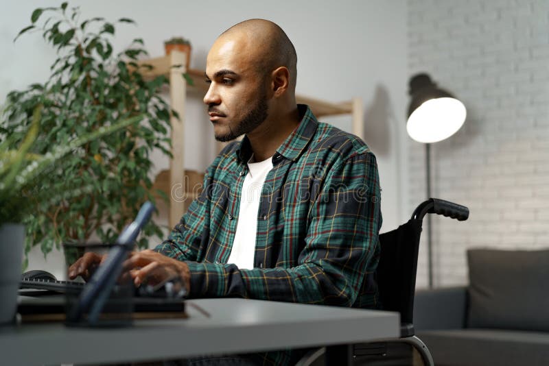 Disabled Young African American Man in Wheelchair Using Computer while ...