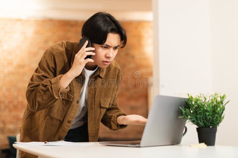 Asian Guy Talking on Phone Having Problems with Laptop Indoors Stock ...