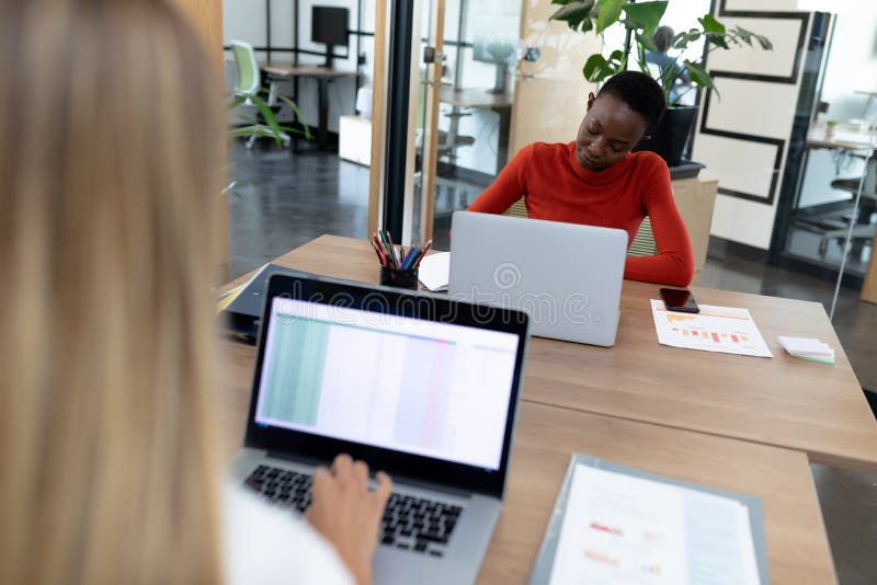 Diverse Female Business Colleagues Sitting at Desks Using Laptop Making ...