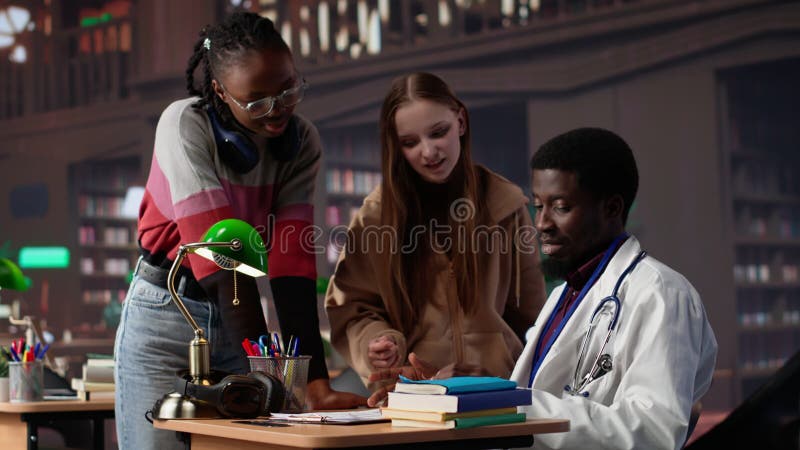 Diverse Group of Pupils in a Library Discuss with a Medic Resident ...