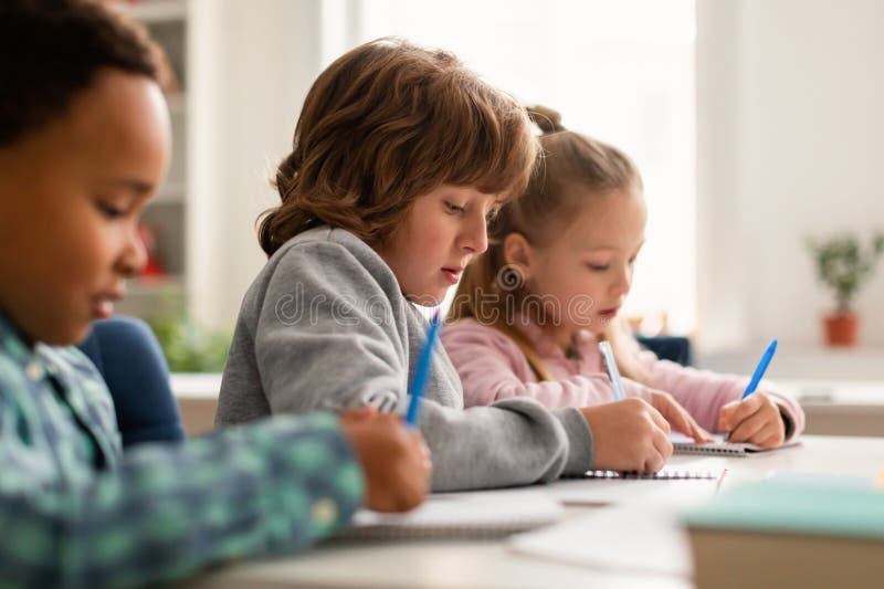 Diverse Pupil Writing during the Lesson at Desk in Classroom at ...