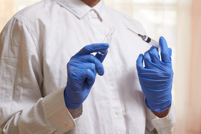 A Doctor In Blue Medical Gloves And A White Lab Coat Holds A Syringe