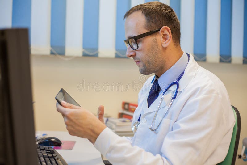 A Doctor on Duty Working in His Oficee on a Computer (pc) and Ta Stock ...