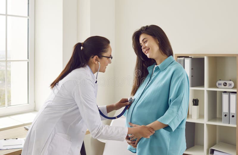 Doctor Obstetrician With Stethoscope Examines Happy Young Pregnant