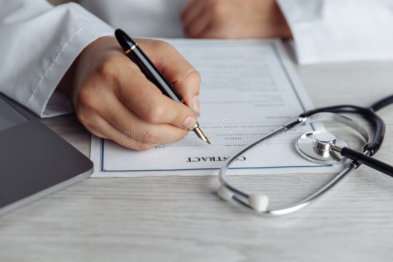Doctor is Sitting at Table and Signing Medical Document in Office Stock ...
