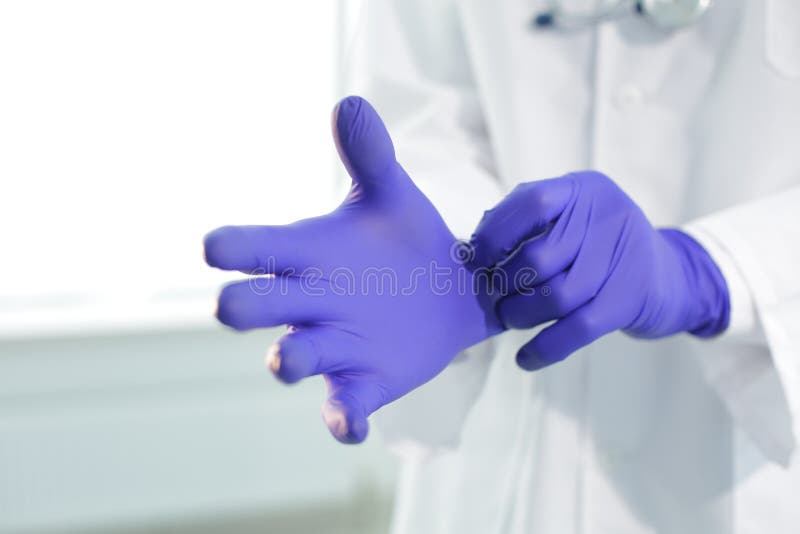 Doctor With Stethoscope In A Medical Gown Puts On Protective Gloves In