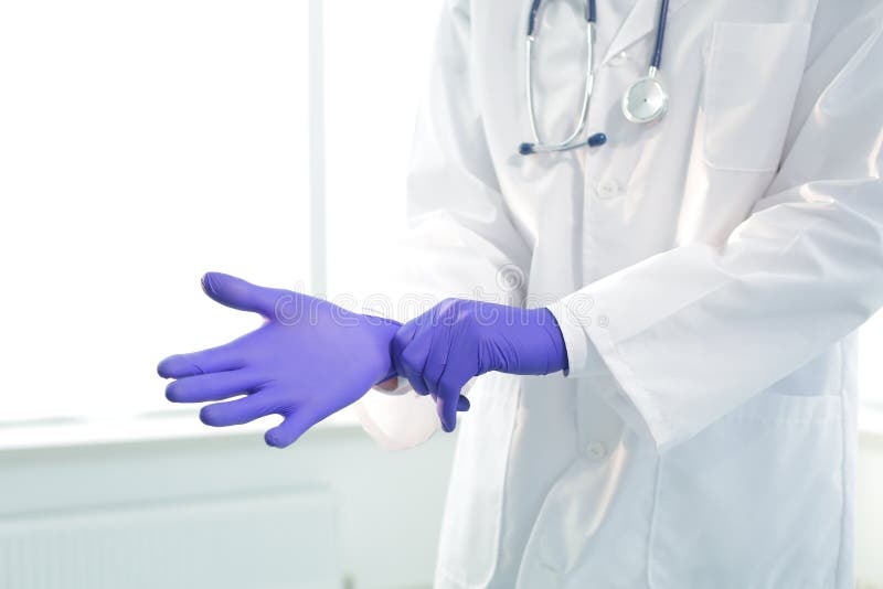 Doctor With Stethoscope In A Medical Gown Puts On Protective Gloves In