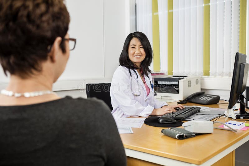 Doctor Using Computer while Looking at Patient at Desk Stock Photo ...