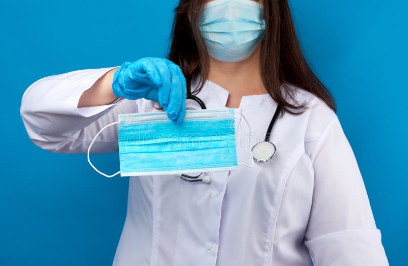 Doctor in a White Coat and Mask Holds a Stack of Protective Disposable ...