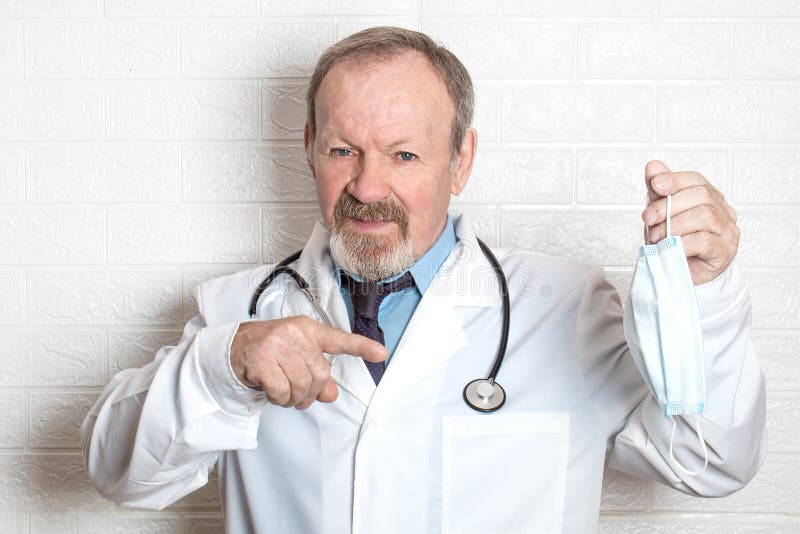 A Doctor Holds a Mask in One Hand, and Points at it with the Other ...