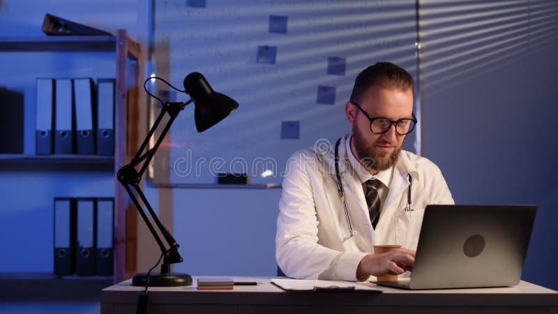 Doctor in White Lab Coat Sitting at Table and Using Laptop during Night ...