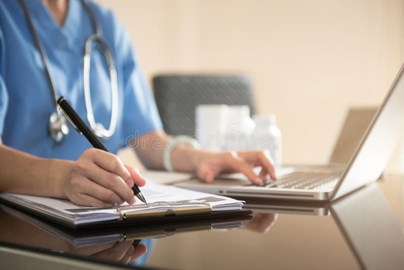 Doctor Working with Laptop Computer and Writing on Paperwork Stock ...