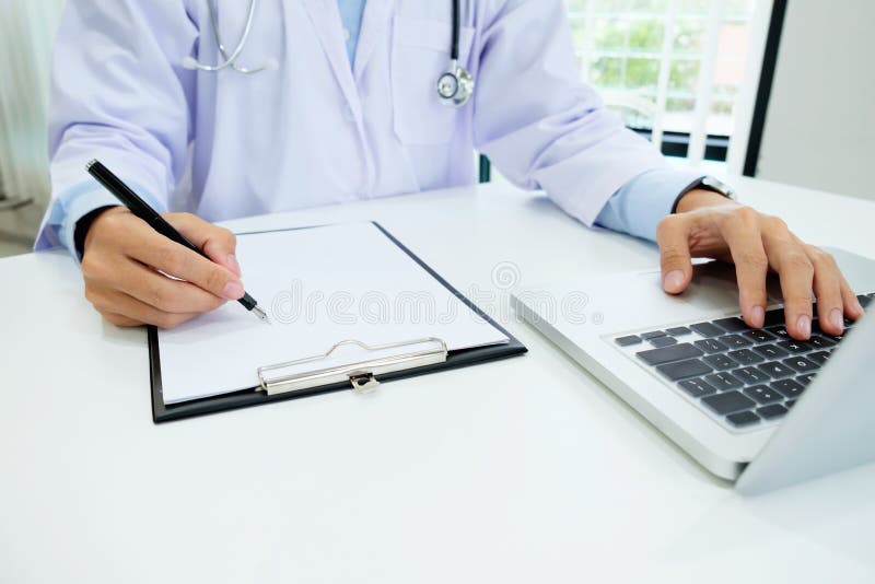 Doctor Working with Laptop Computer and Writing on Paperwork Stock ...