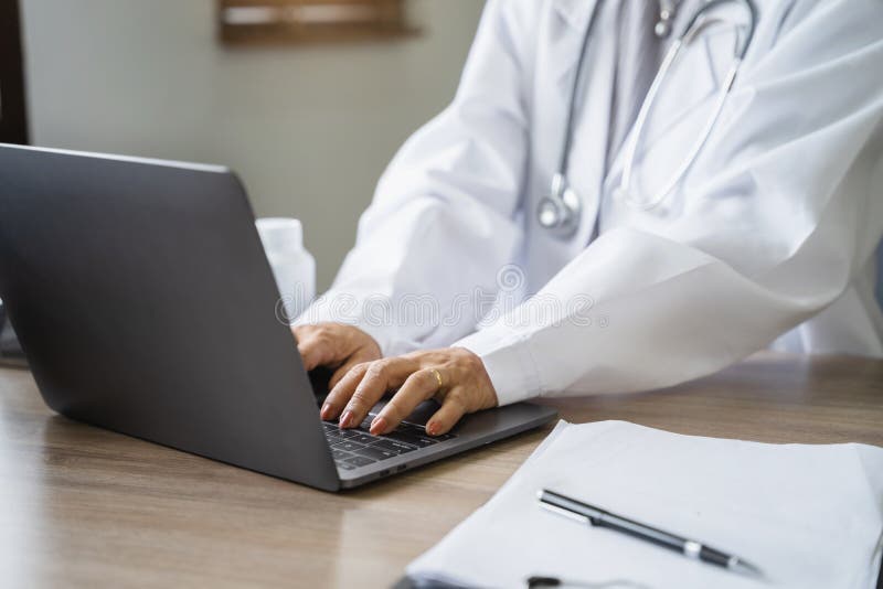 Doctor Working with Laptop Computer and Writing on Paperwork. in the ...