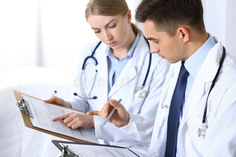 Doctors Writing Papers Using Clipboard. Physicians Discussing ...