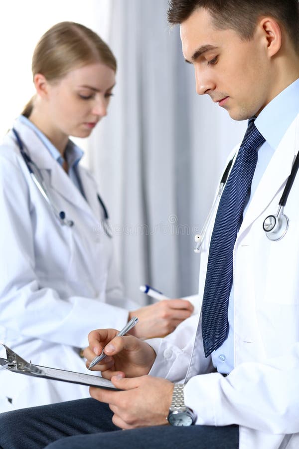 Doctors Writing Papers Using Clipboard. Physicians Discussing ...