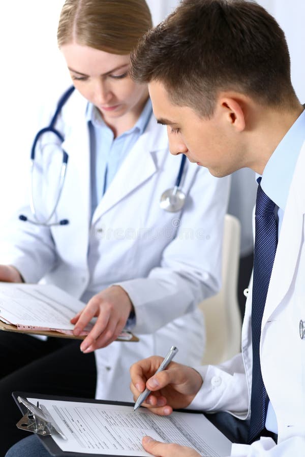 Doctors Writing Papers Using Clipboard. Physicians Discussing ...