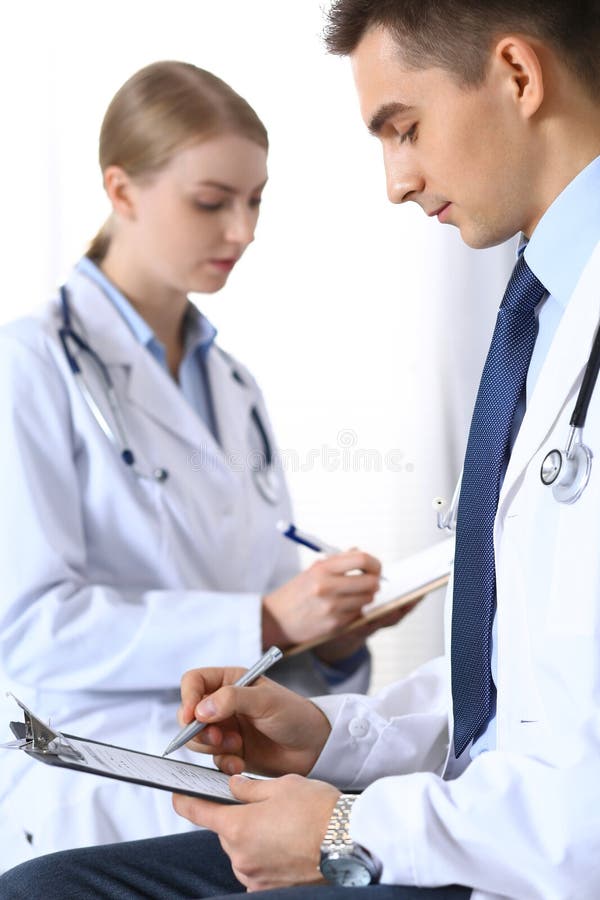 Doctors Writing Papers Using Clipboard. Physicians Discussing ...