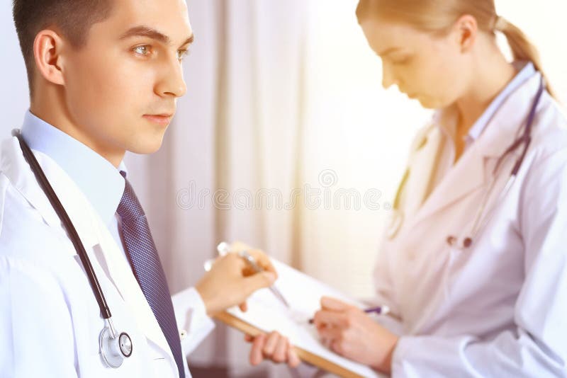 Doctors Writing Papers Using Clipboard. Physicians Discussing ...
