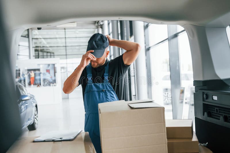 With Document. Delivery Man in Uniform is Indoors with Car and with ...
