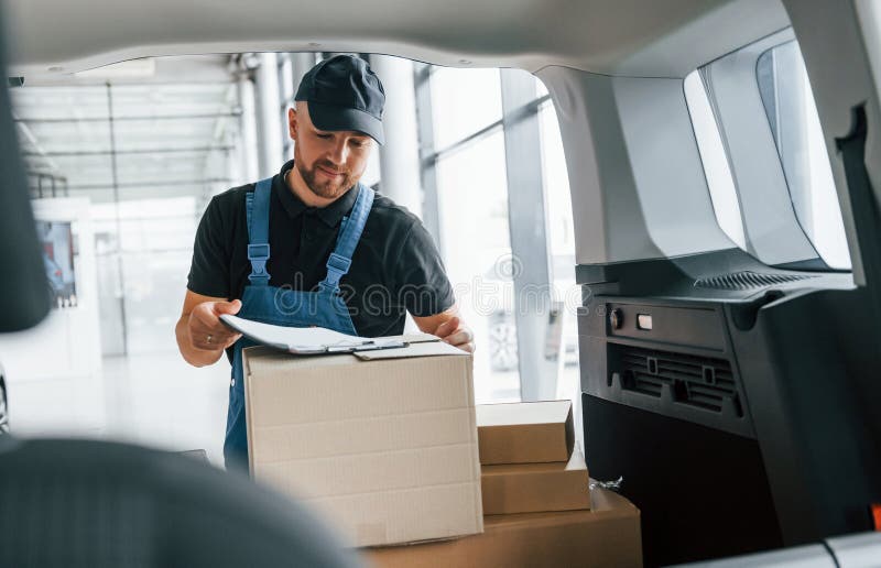 With Document. Delivery Man in Uniform is Indoors with Car and with ...