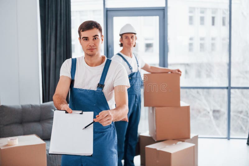 Document To Sign. Two Young Movers in Blue Uniform Working Indoors in ...