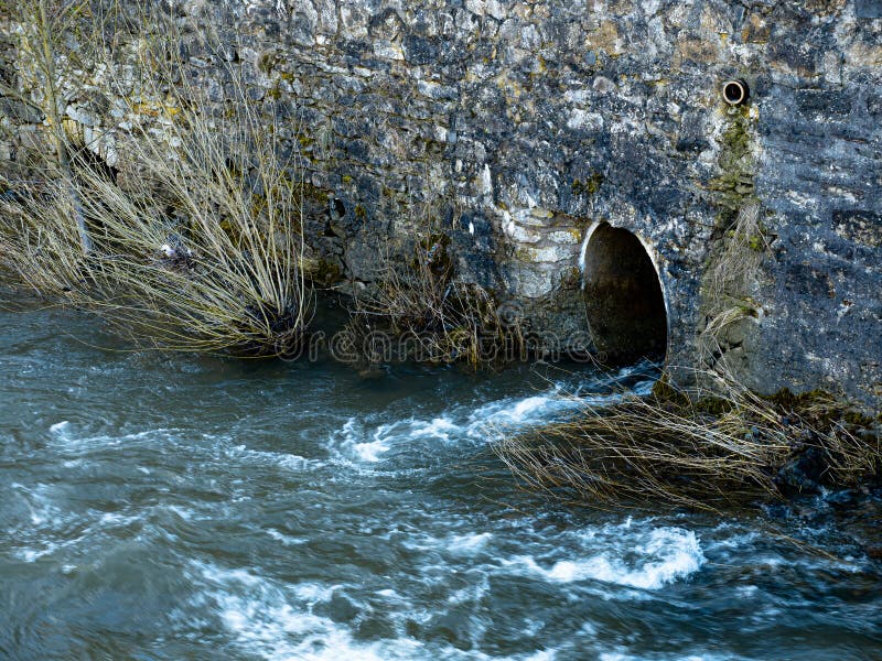A Drain that is Embedded in a Wall and Flows into a River Stock Photo ...
