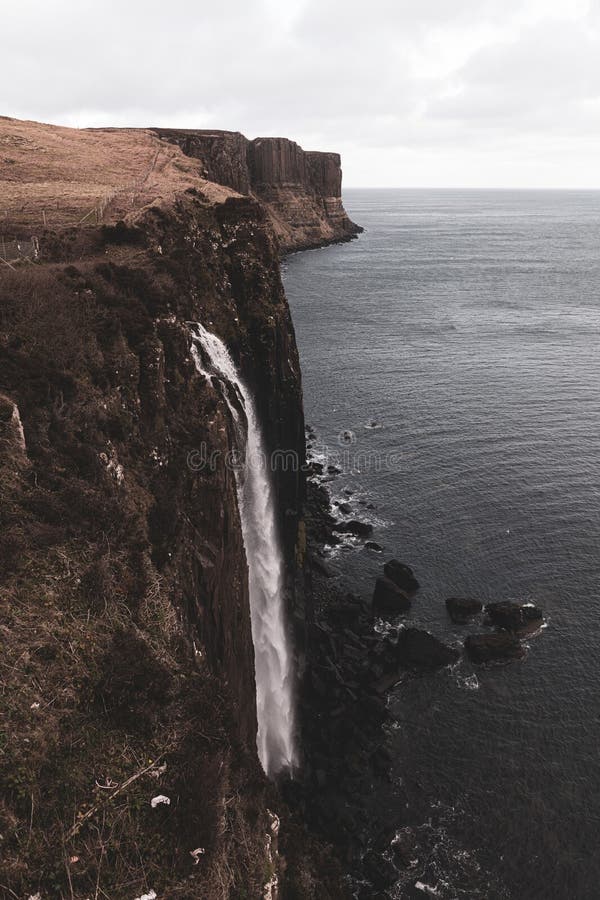 Dramatic Coastal Cliff with a Waterfall Cascading into the Ocean Under ...