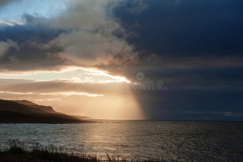 Dramatic Coastal Sunset with Sun Rays Piercing through Dark Clouds ...