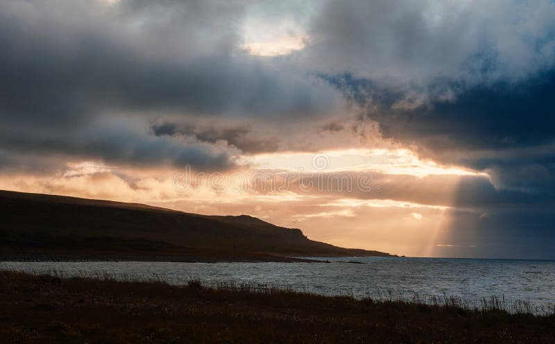 Dramatic Coastal Sunset with Sun Rays Piercing through Dark Clouds ...