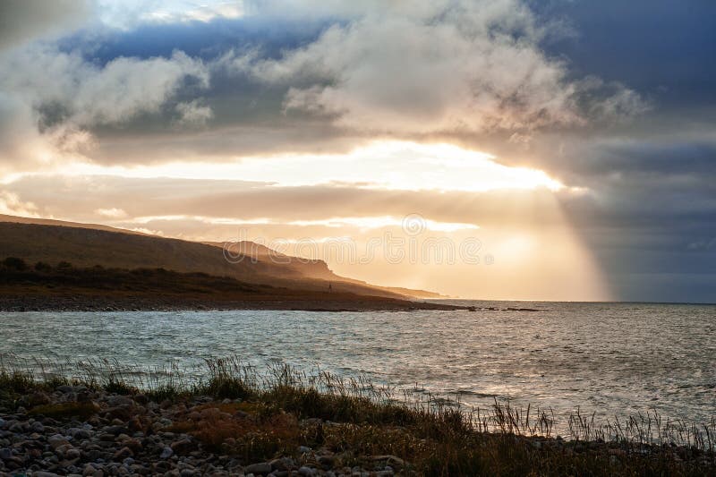 Dramatic Coastal Sunset with Sun Rays Piercing through Dark Clouds ...