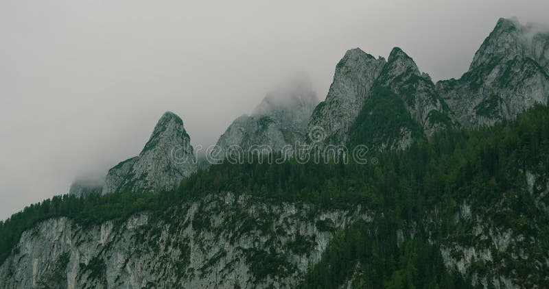 Dramatic Mountain Peaks Covered in Mist with Green Forests Below Under ...