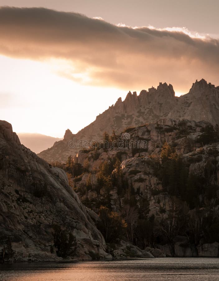 A Dramatic Mountain Range at Sunrise with Trees, a Lake and Clouds in ...