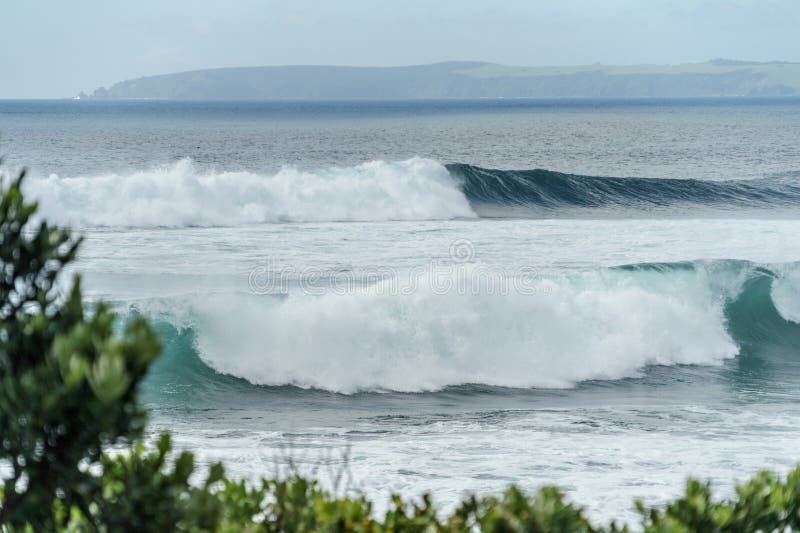 Dramatic Shot of Wavy Ocean with Mountains in the Distance and Green ...