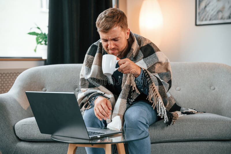 Drinking a Tea. Sick Man is Sitting on the Sofa at Home by the Laptop ...
