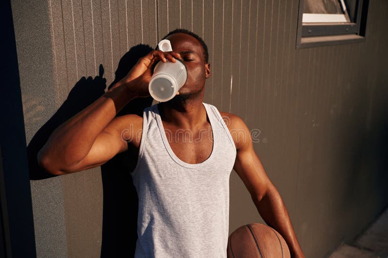 Drinking the Water. Young Black Man is with Basketball Ball Outdoors ...