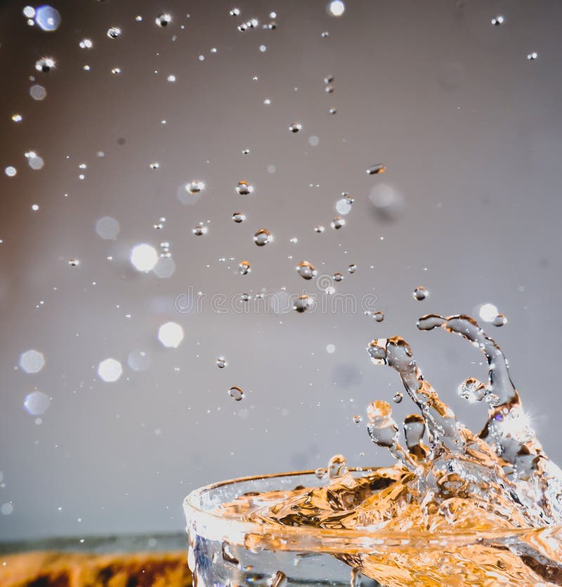 A Drop Splashing in Orange Water, Falling into the Water Against a Gray ...