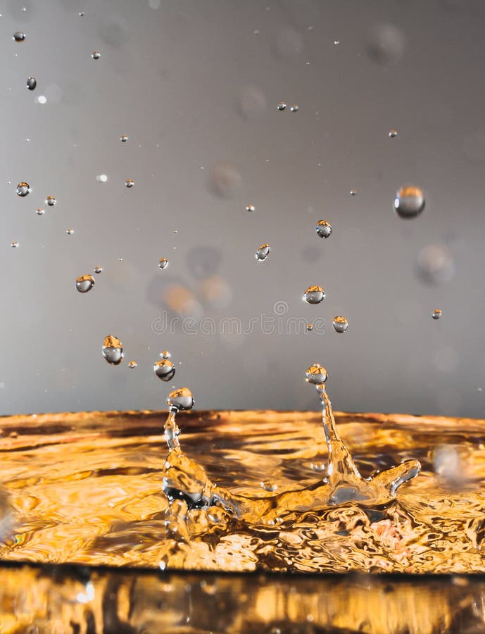 A Drop Splashing in Orange Water, Falling into the Water Against a Gray ...